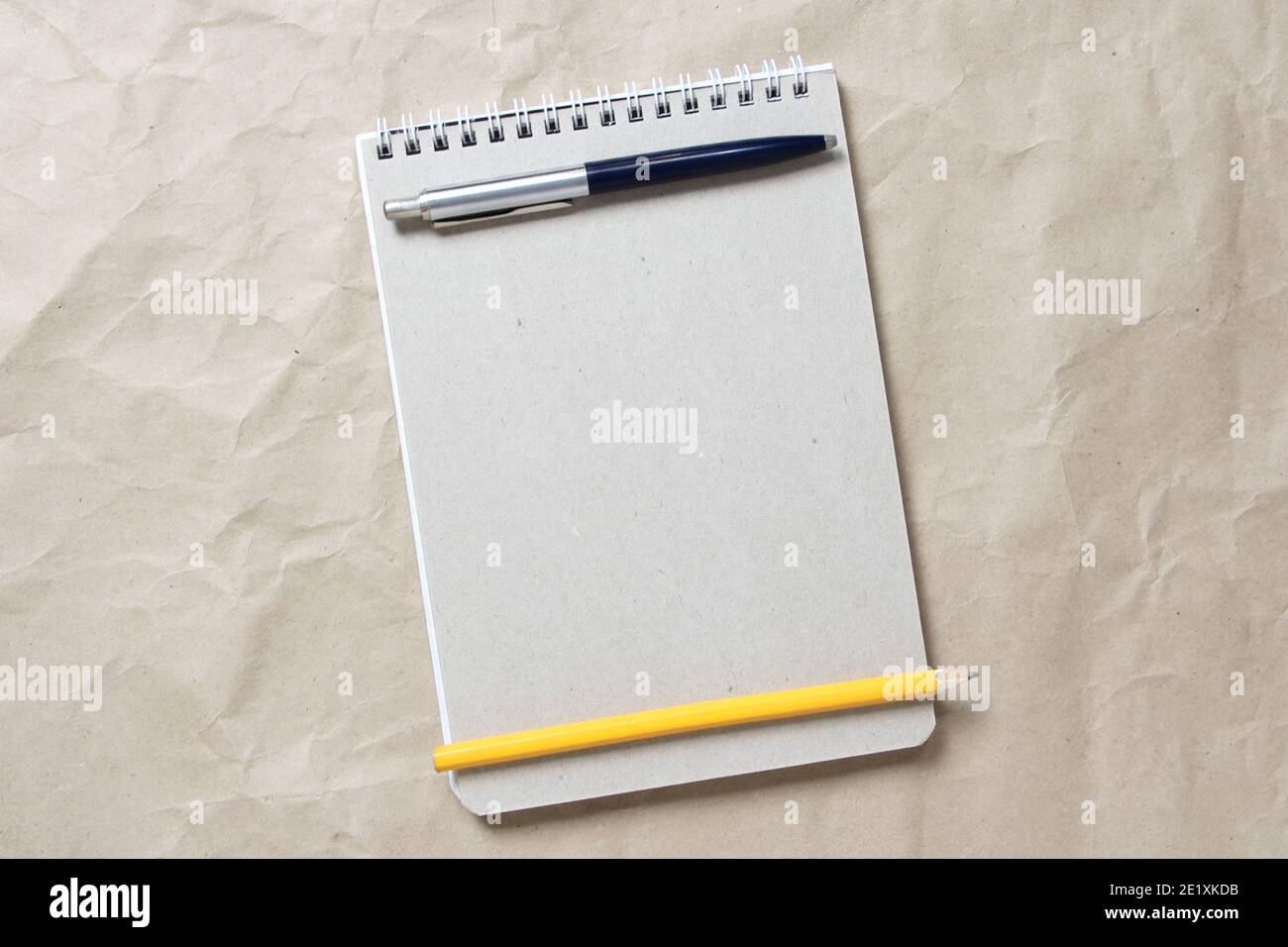 Gray notepad with white coiled spring and pen and pencil on a ...