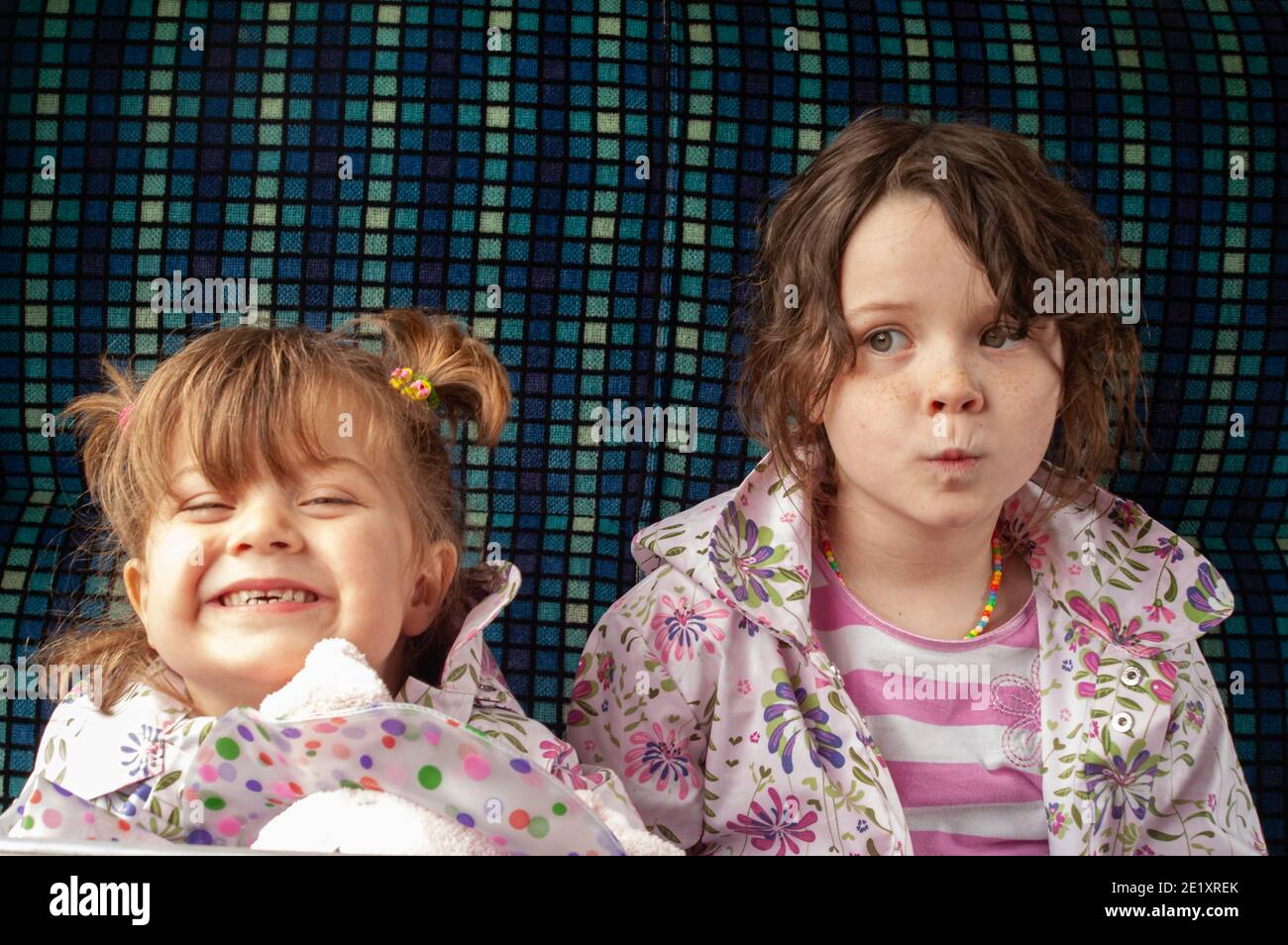 Two young girls dressed in pink on a blue chequered train seat one ...