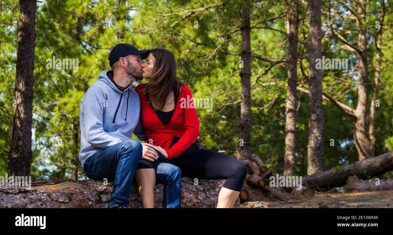 Young couple seated on tree trunk at forest kissing. Affectionate man ...