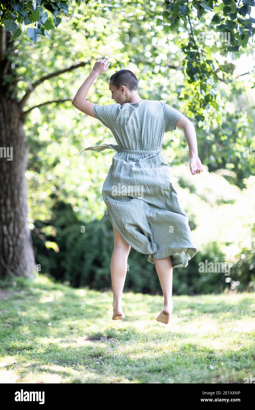Non-binary shaved head biological female in green dress jumping on ...