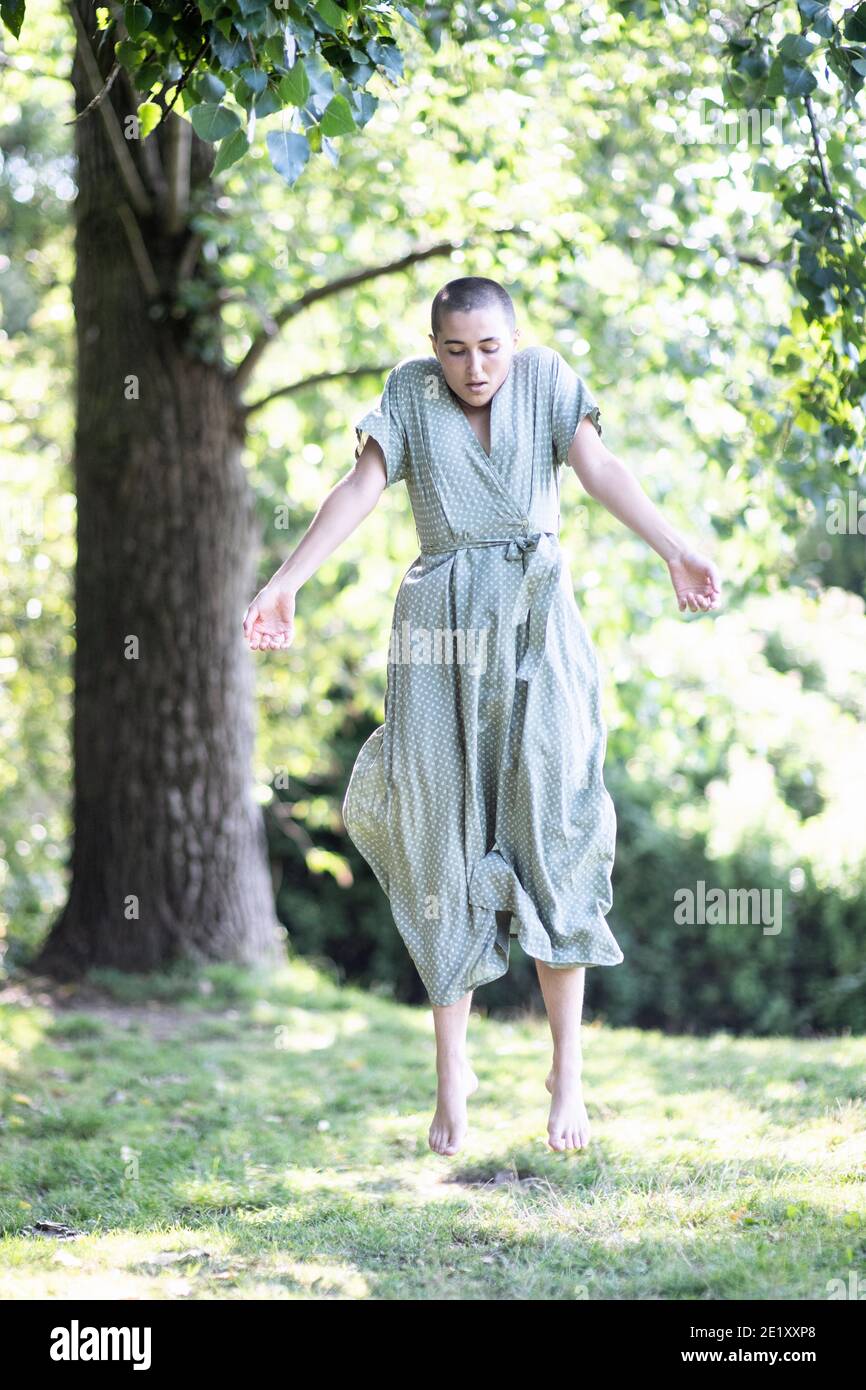 Non-binary shaved head biological female in green dress jumping on ...
