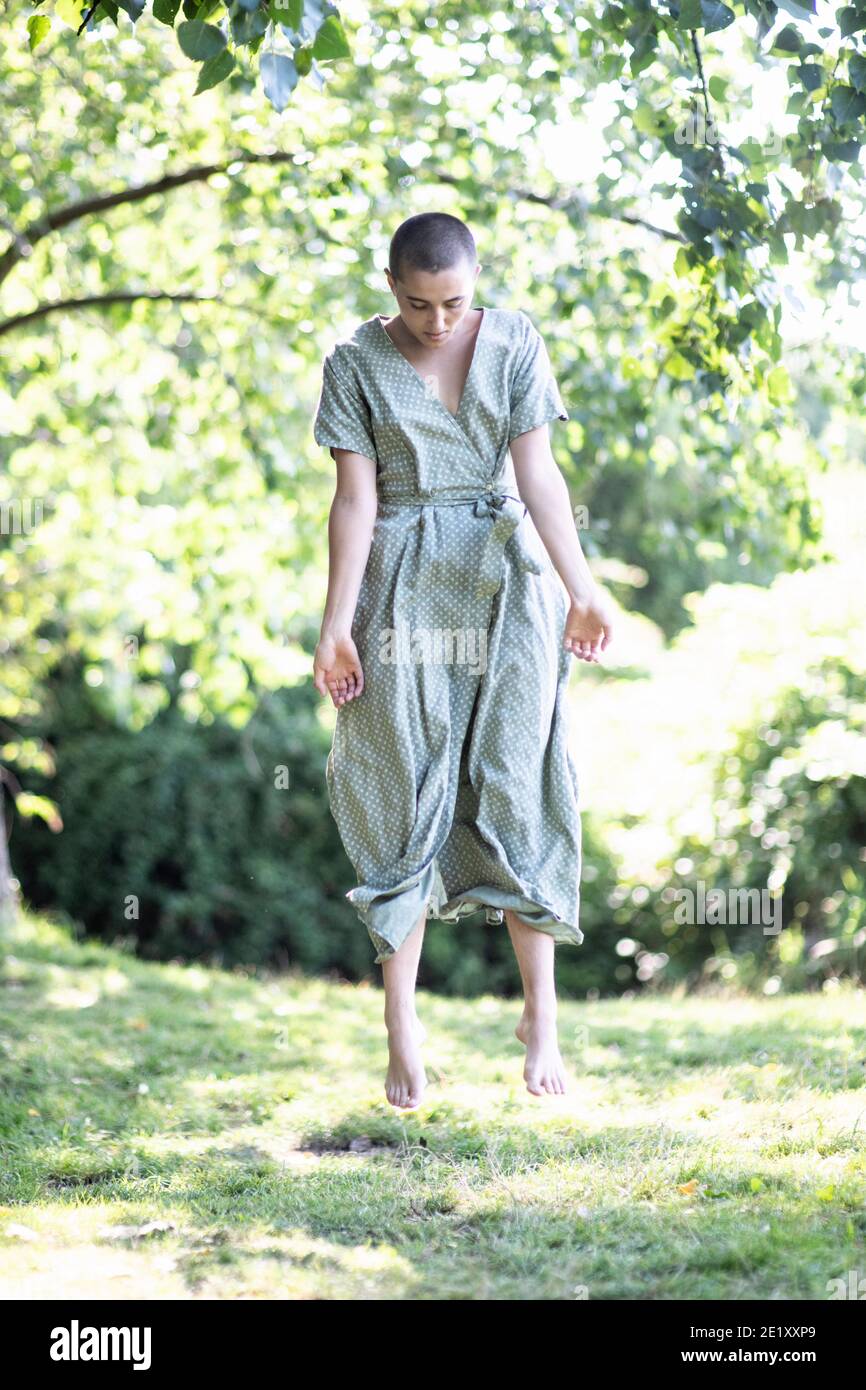 Non-binary shaved head biological female in green dress jumping on ...