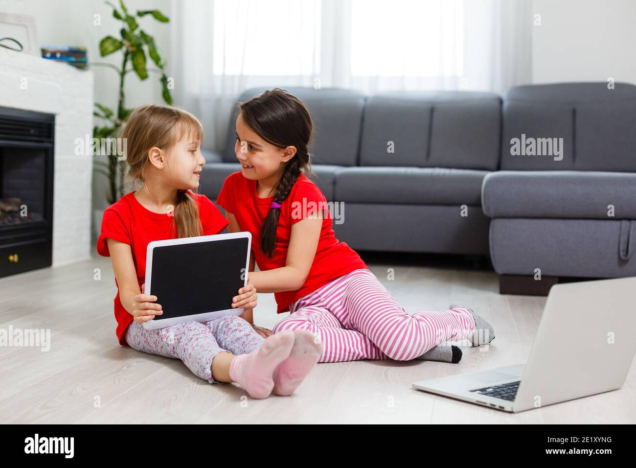 Little girls playing on a tablet computing device sitting on the floor ...