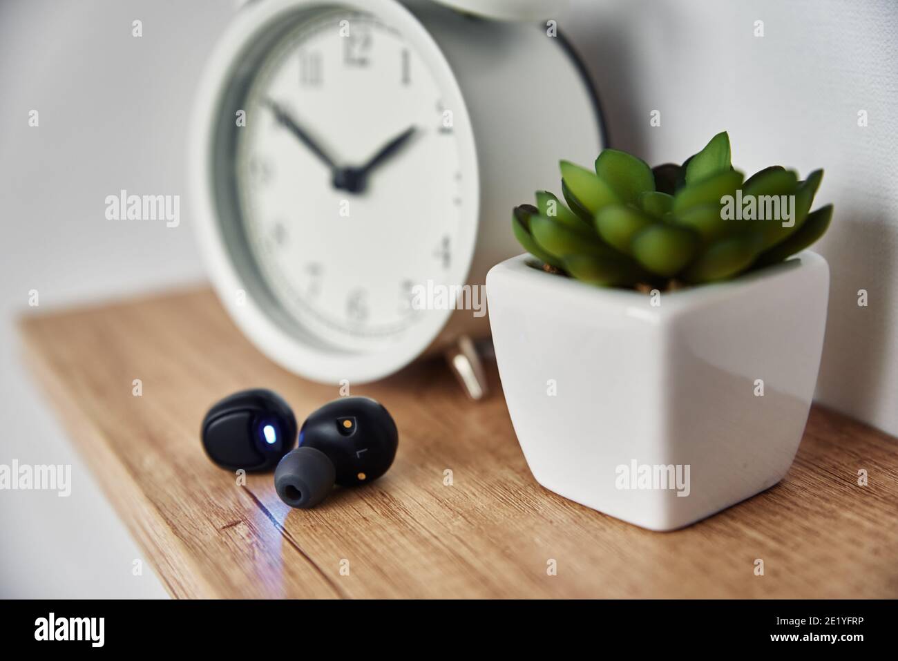 Wireless earphones on the shelf with alarm clock and house plant ...