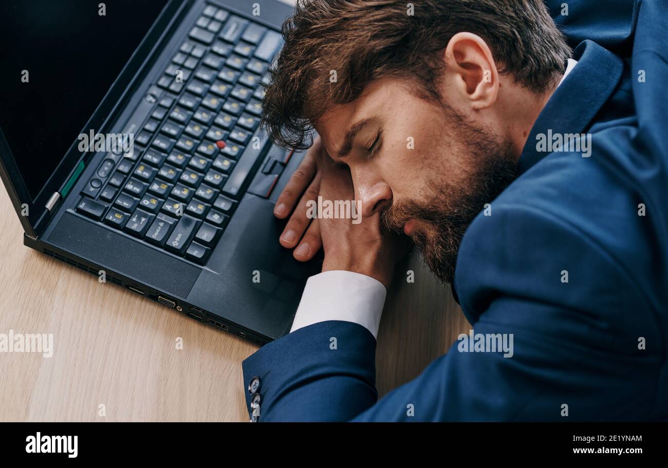 Man in a suit at a working table in front of a laptop office tired ...