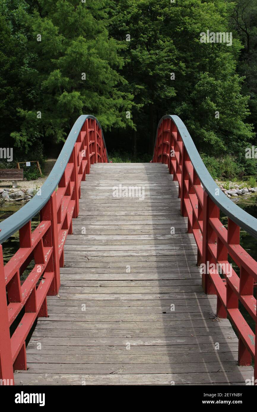 A wood arch bridge, with red side railings, over a lake leading the a ...
