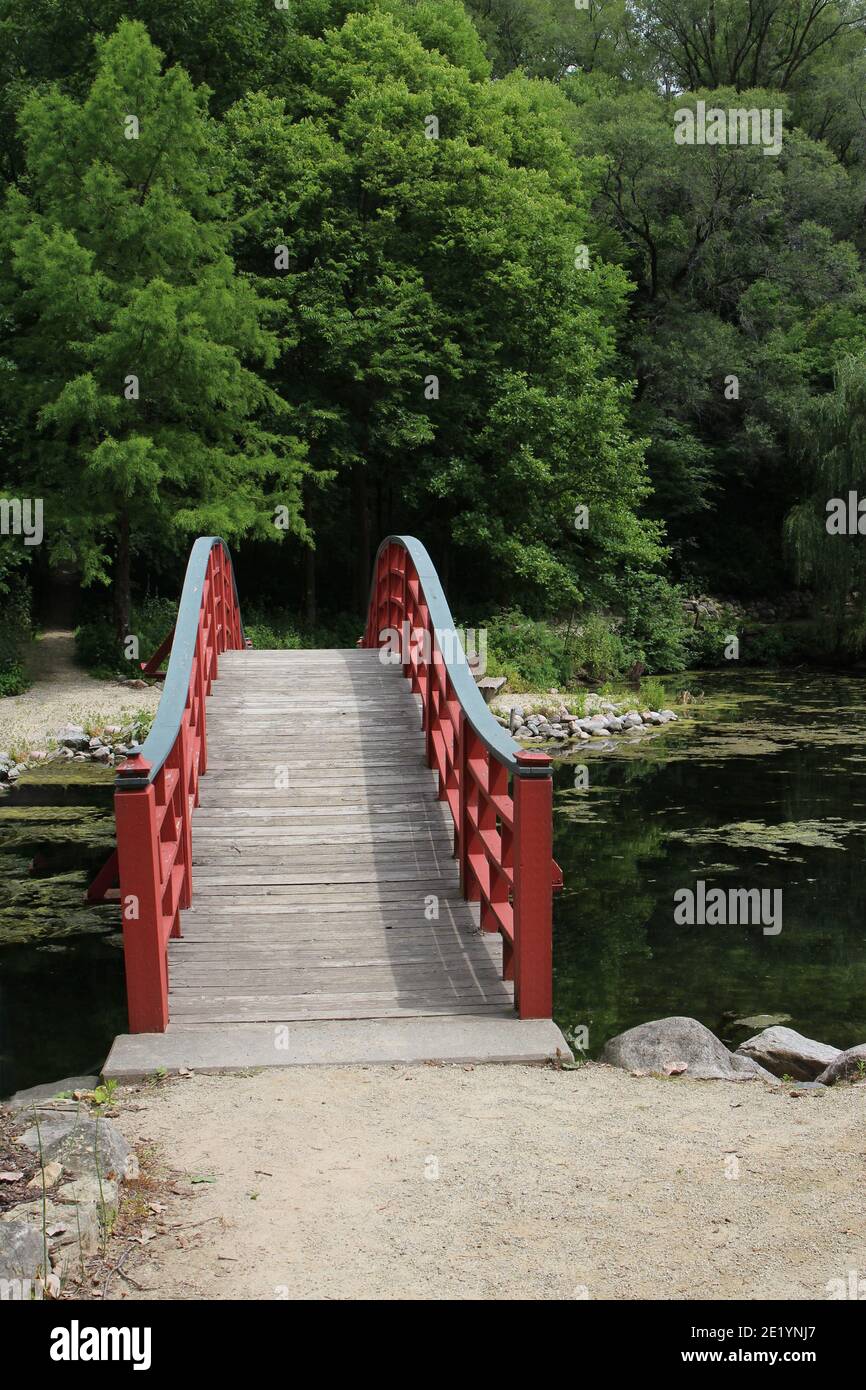 A wood arch bridge, with red side railings, over a lake leading the a ...