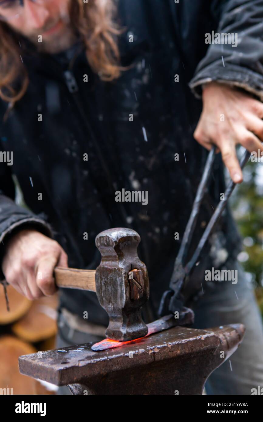 Close up shot of a young blacksmith hammering a red, sizzling hot rod ...