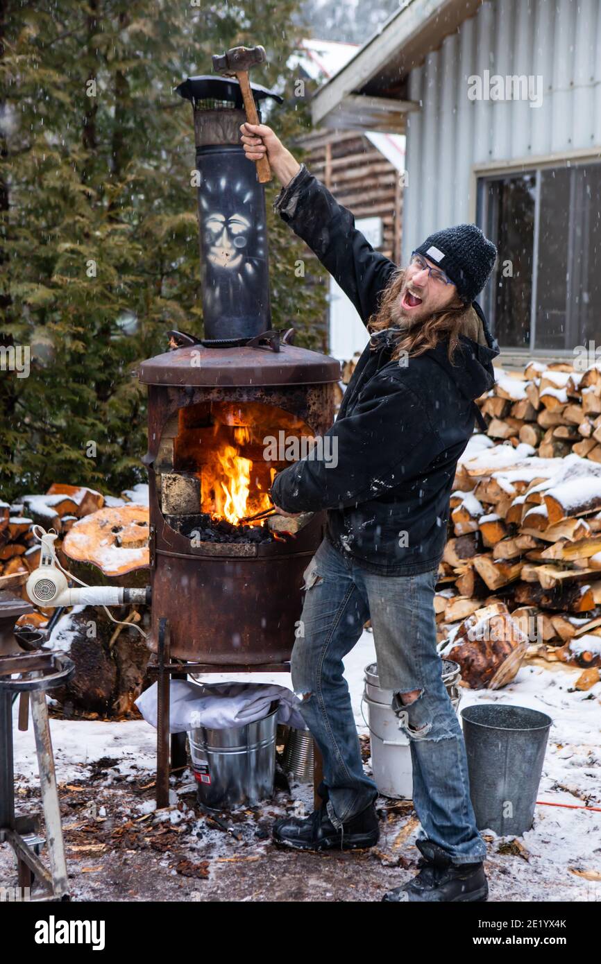 Young man playing with a forge and raising a hammer, laughing and ...
