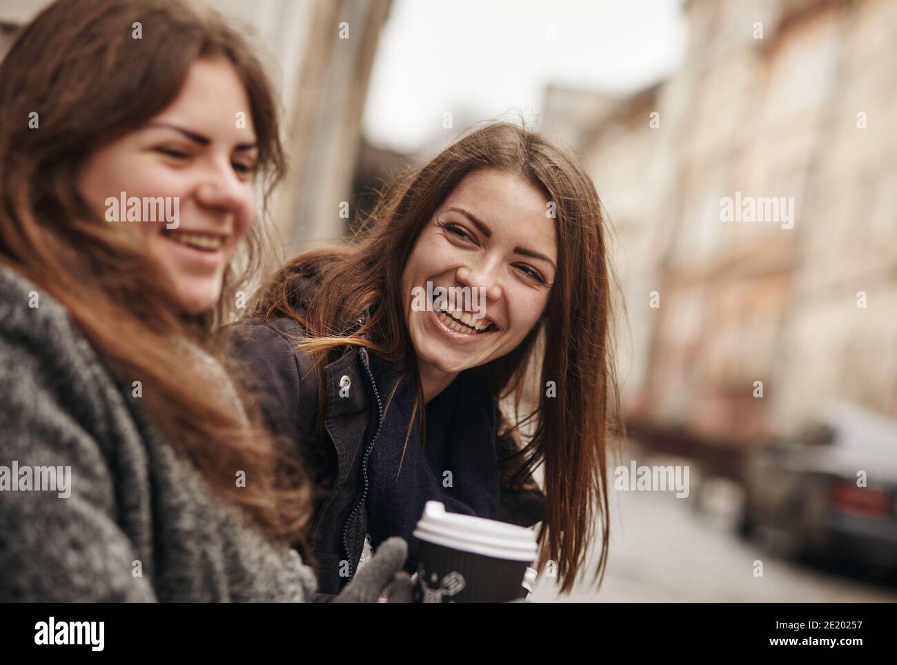 Outdoors fashion portrait of two young beautiful women friends drinking ...