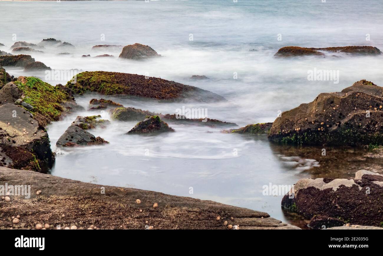 A Long-exposure photo of the water washing up on the rocks Stock Photo ...