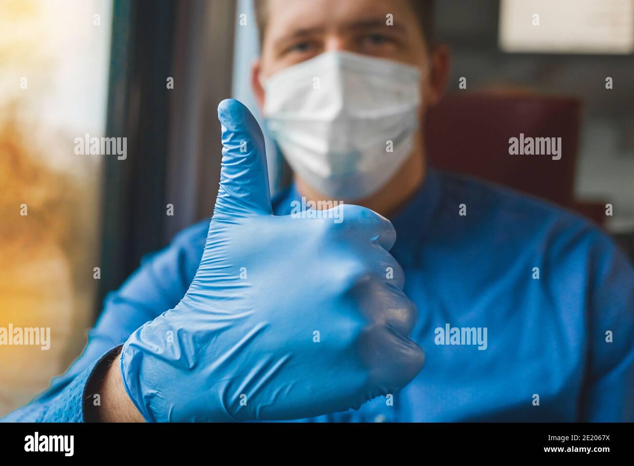 Young guy in a shirt and a medical mask shows a cool thumb up with his ...