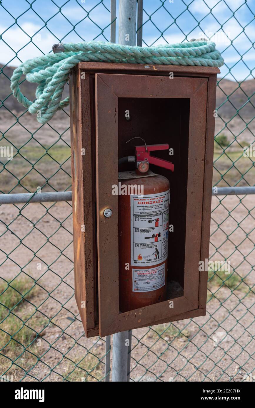 A fire extinguisher in a rusty metal box hangs on a chain link fence ...