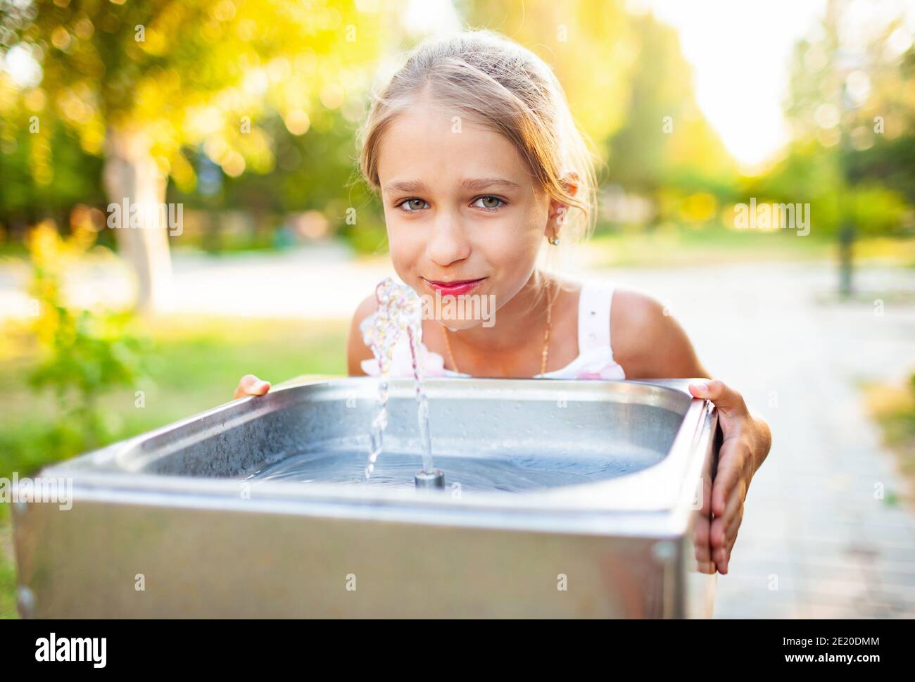 Cheerful wonderful girl drinks cool fresh water from a small fountain ...