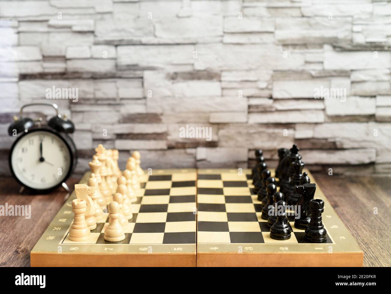 Chess pieces on chess board and alarm clock on wooden table. Blurred ...