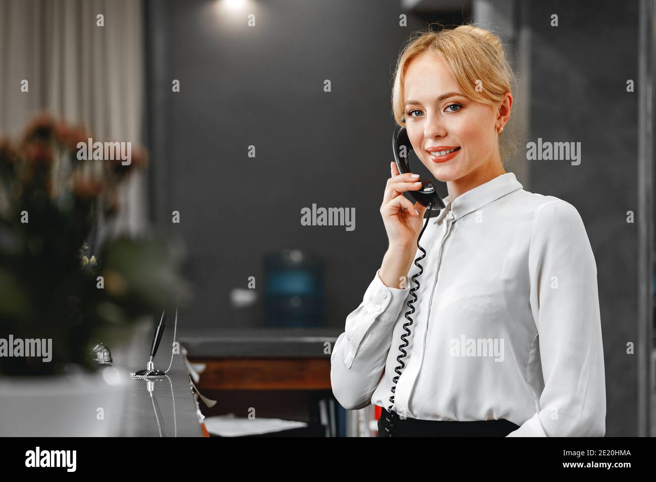 Good-looking friendly woman hotel receptionist talking on the phone ...