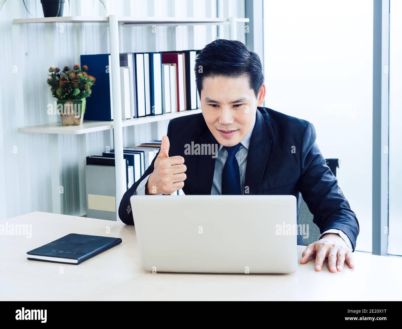 Handsome Asian businessman in suit looking at screen and showing thumb ...