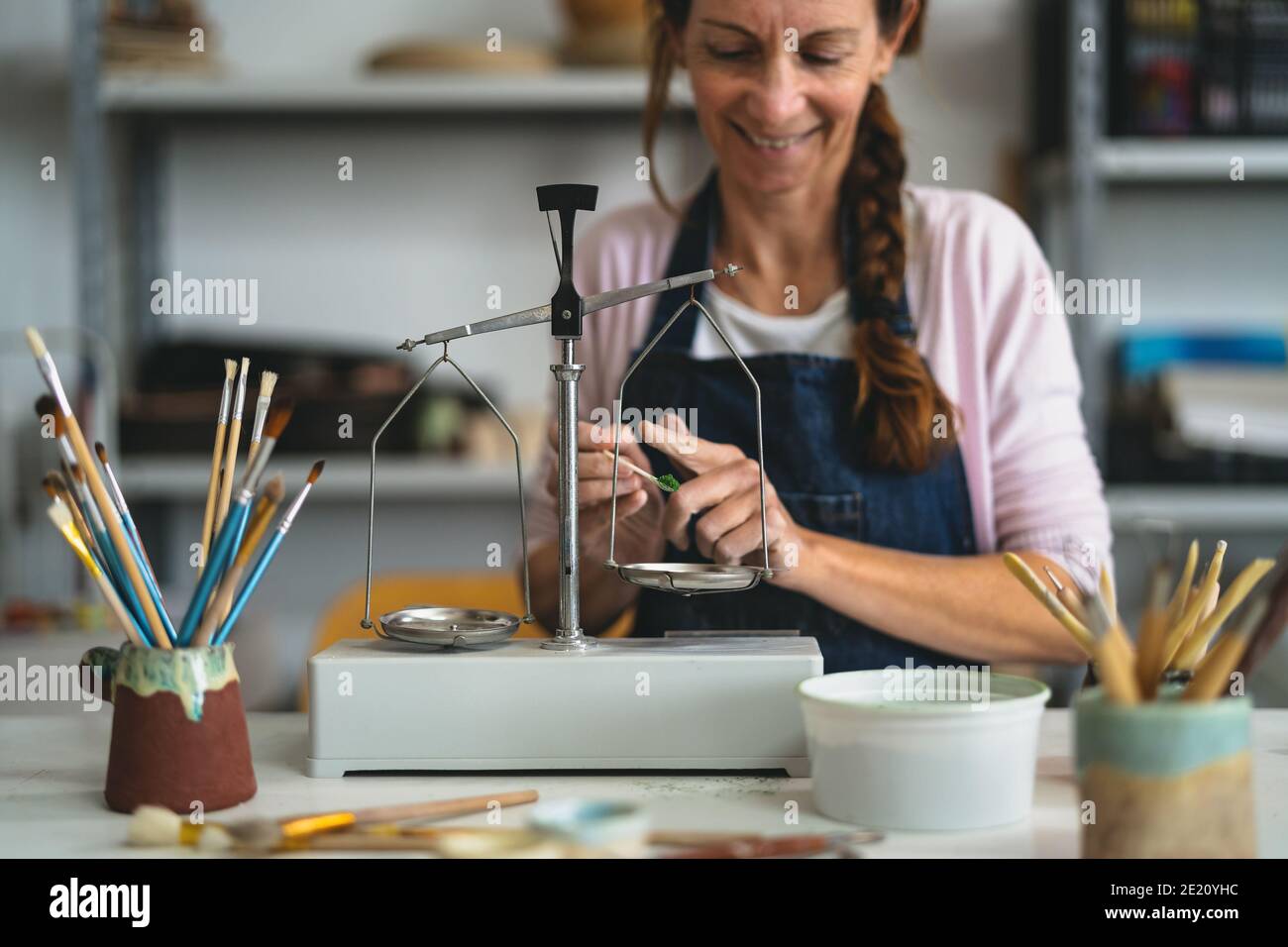 Happy woman pouring paint colors powder on vintage balance in pottery ...