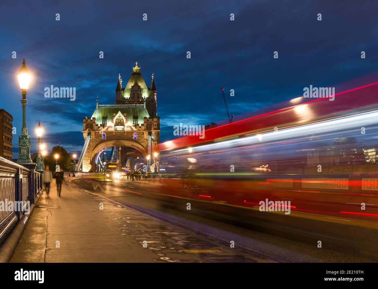 A red bus passing over Tower Bridge at night in London, England, UK ...