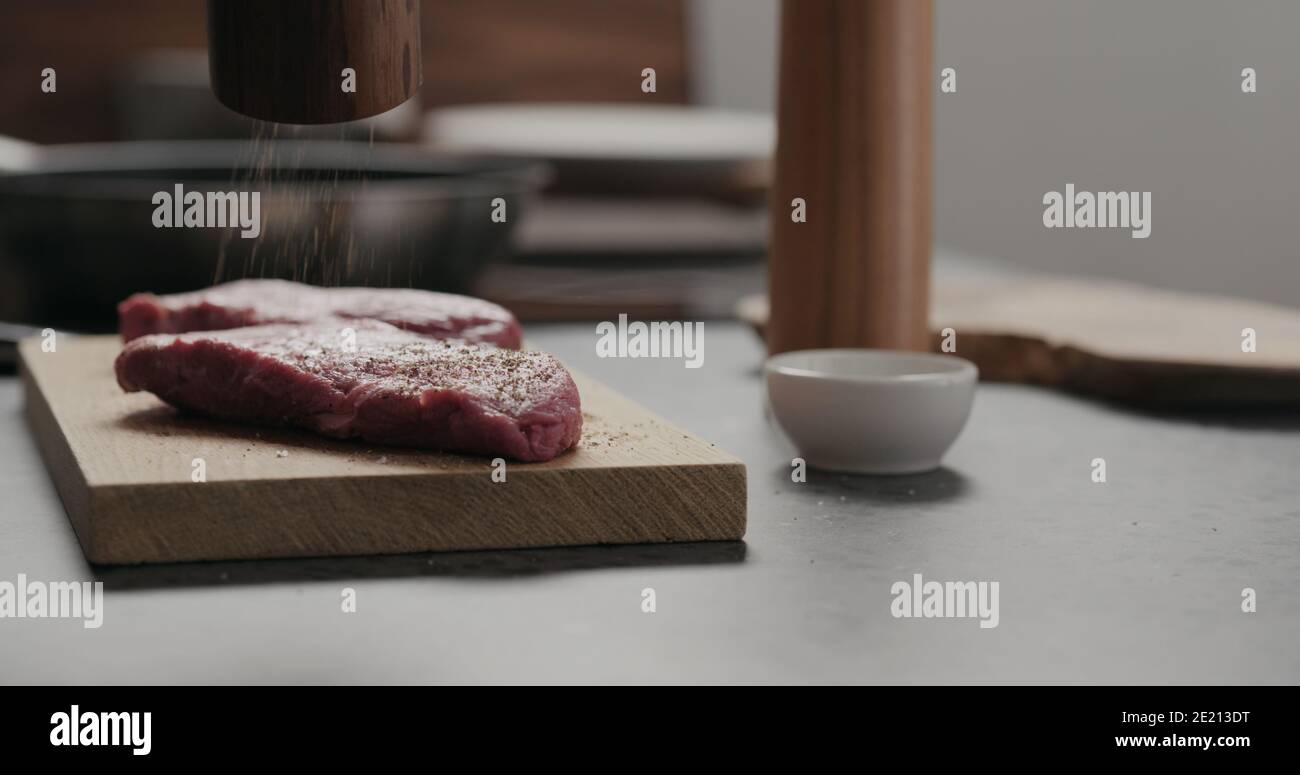 man grinding pepper on raw beef steak on oak board, wide photo Stock ...