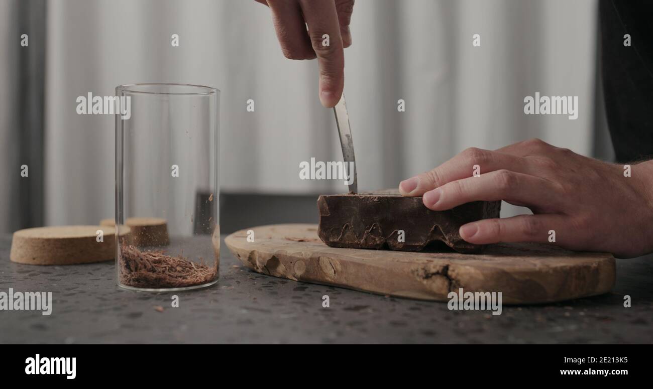 closeup man hands breaking dark chocolate block with knife on wood ...