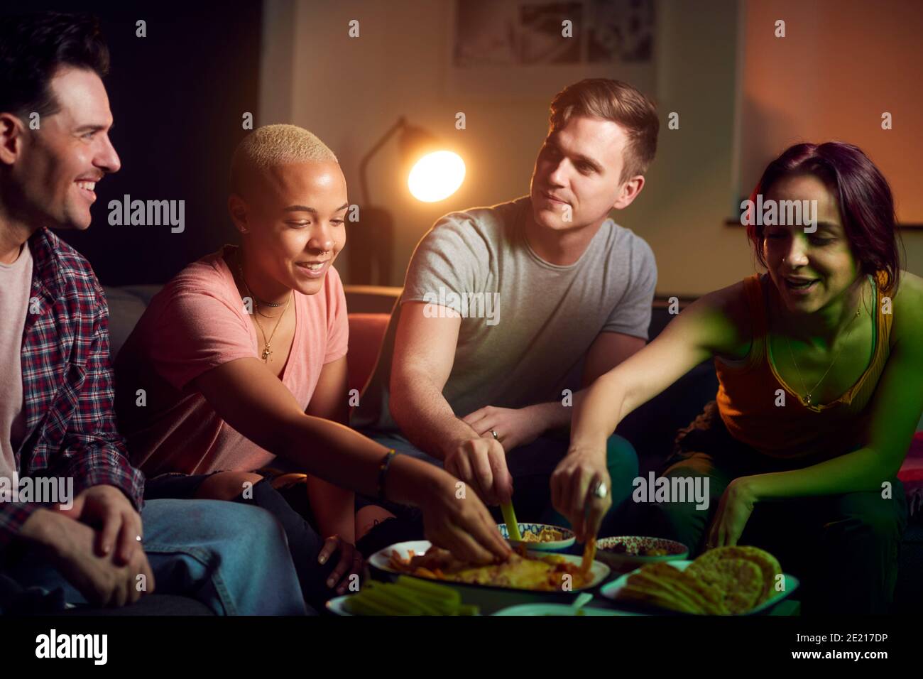 Group Of Friends Eating Dips Sitting On Sofa At Home Relaxing Together ...