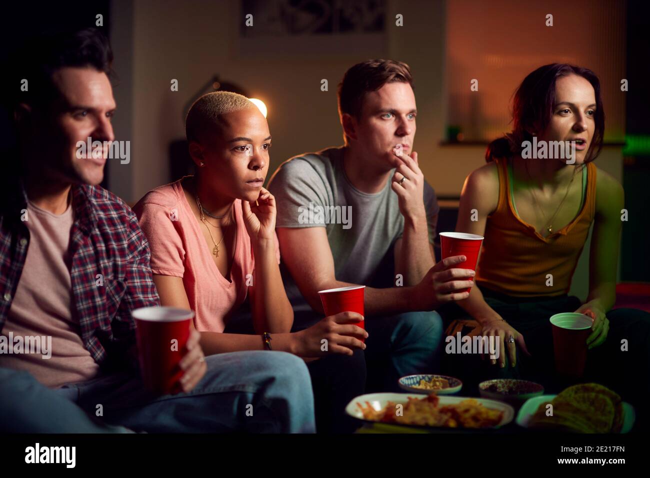 Group Of Friends With Drinks Sitting On Sofa At Home Watching Horror ...