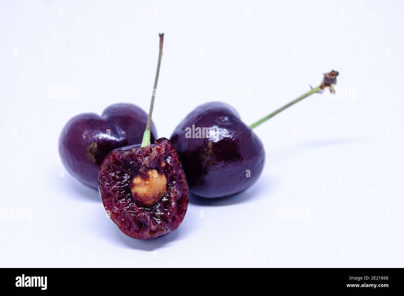 Three cherries isolated against a. white background, One has been ...