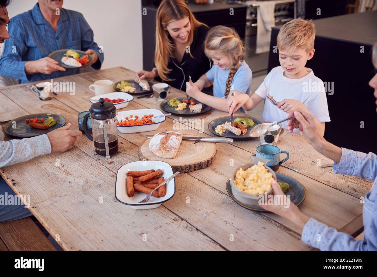 Multi-Generation Family Sitting Around Table At Home In Pyjamas ...