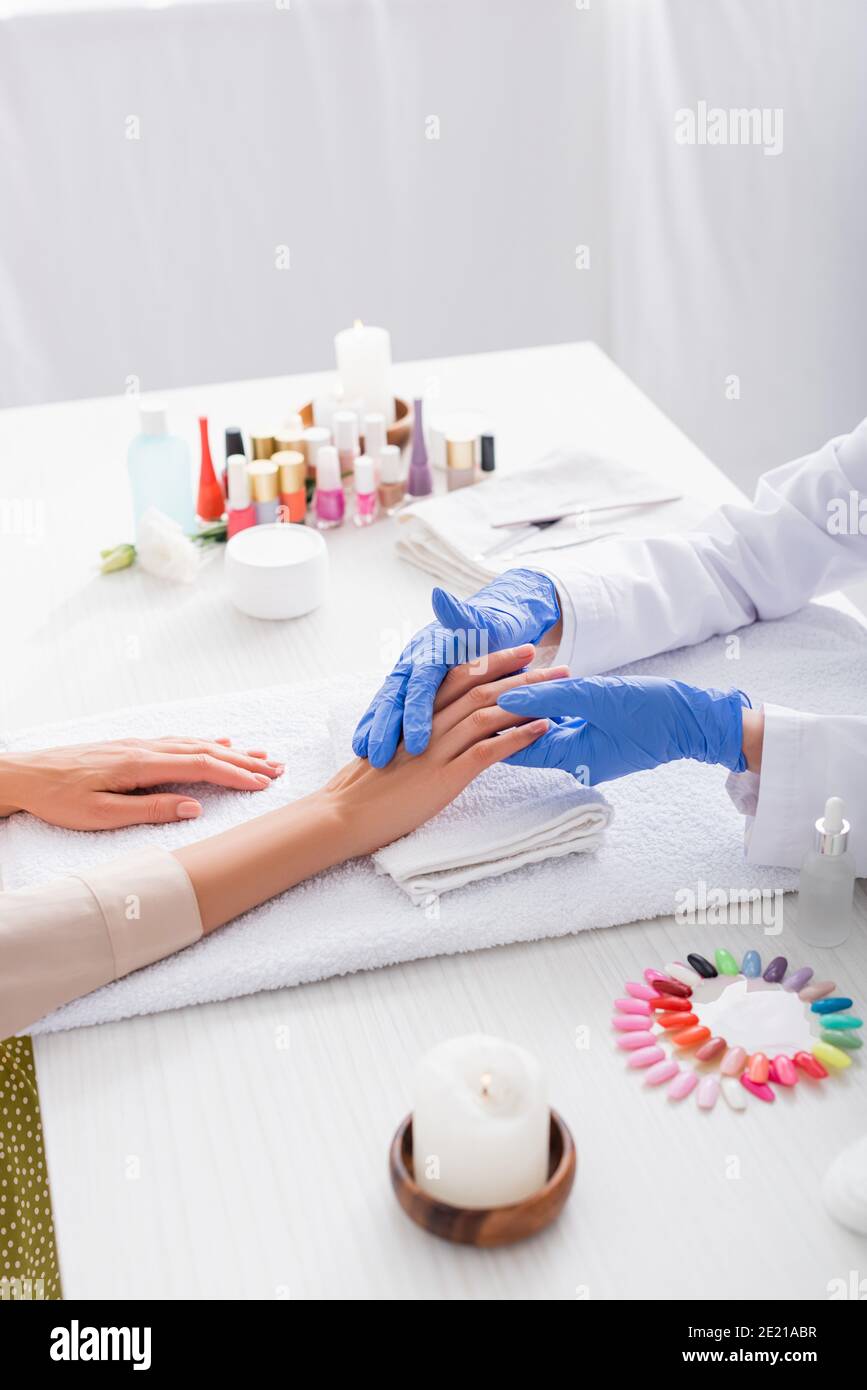 partial view of manicurist touching hand of client near vials of nail ...