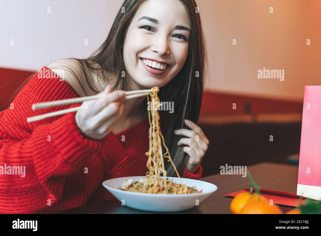 Beautiful smiling young asian woman in red clothes eating noodles with ...