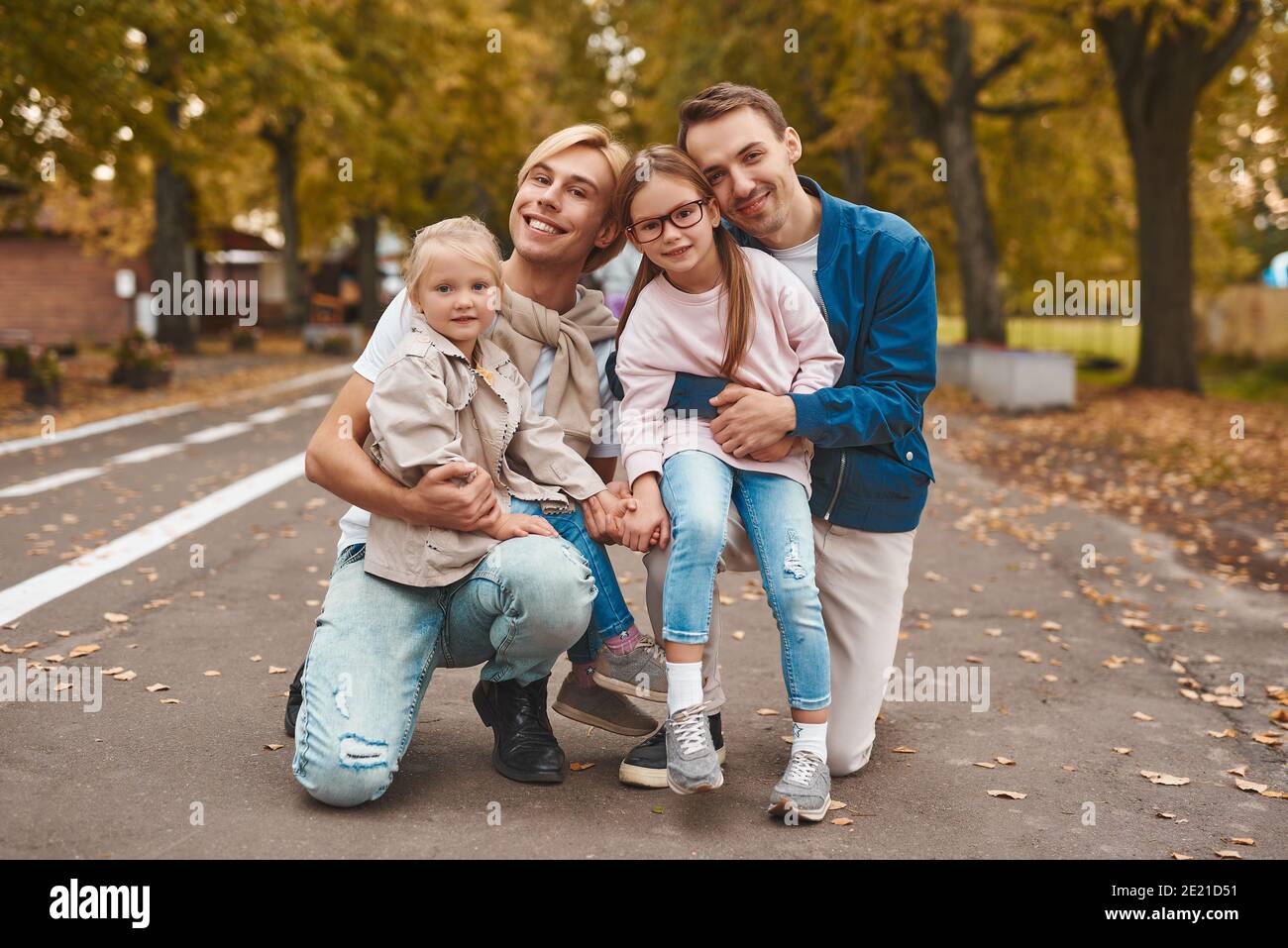 Two gay parents with their adopted daughters walking in park together ...