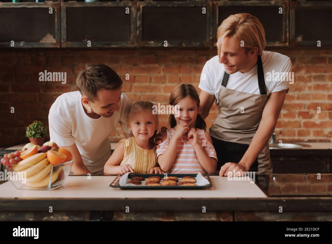 Gay couple with their adopted cute daughters cooking on kitchen. Lgbt ...