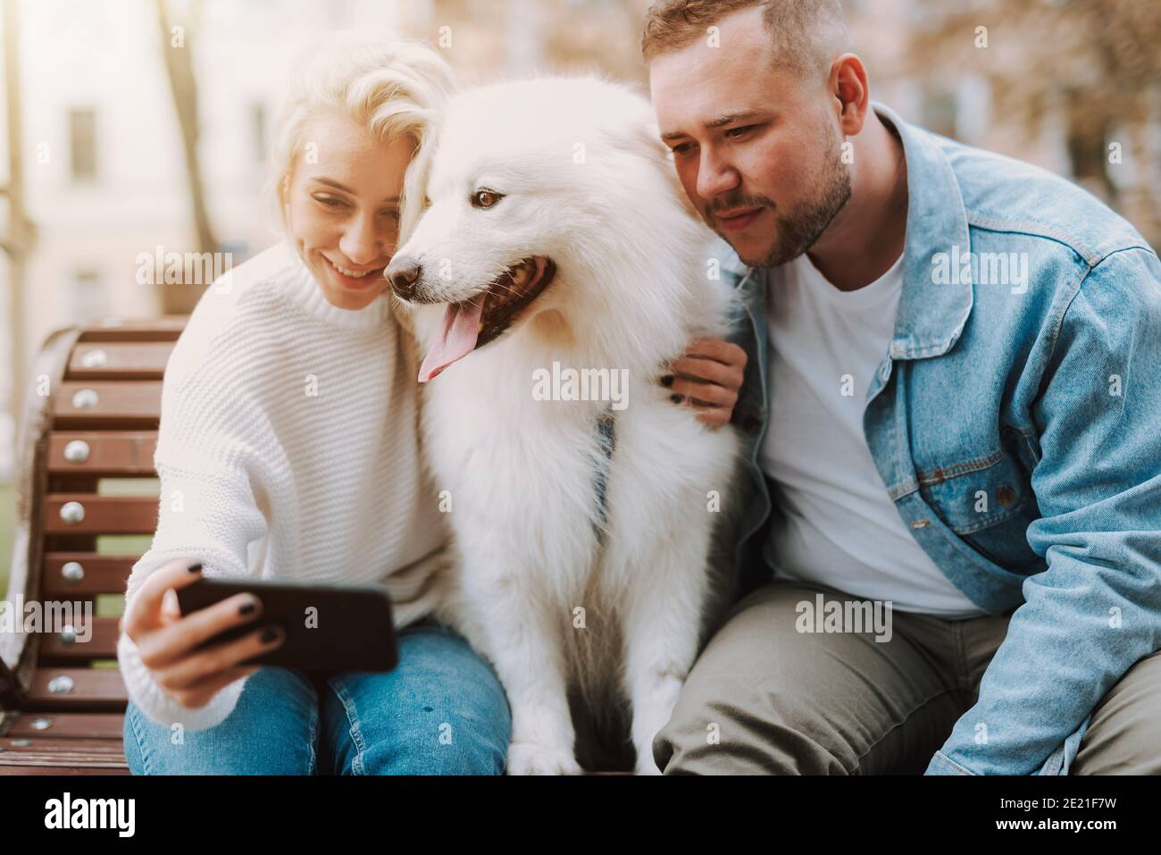 Smiling woman and man sitting on an alley bench with white fluffy puppy ...