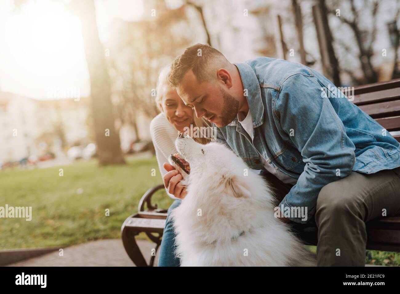 Young happy smiling woman and man are stroking their white fluffy dog ...