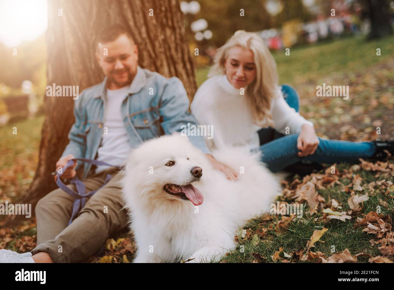 Happy smiling husband and wife with white furry puppy sitting under ...