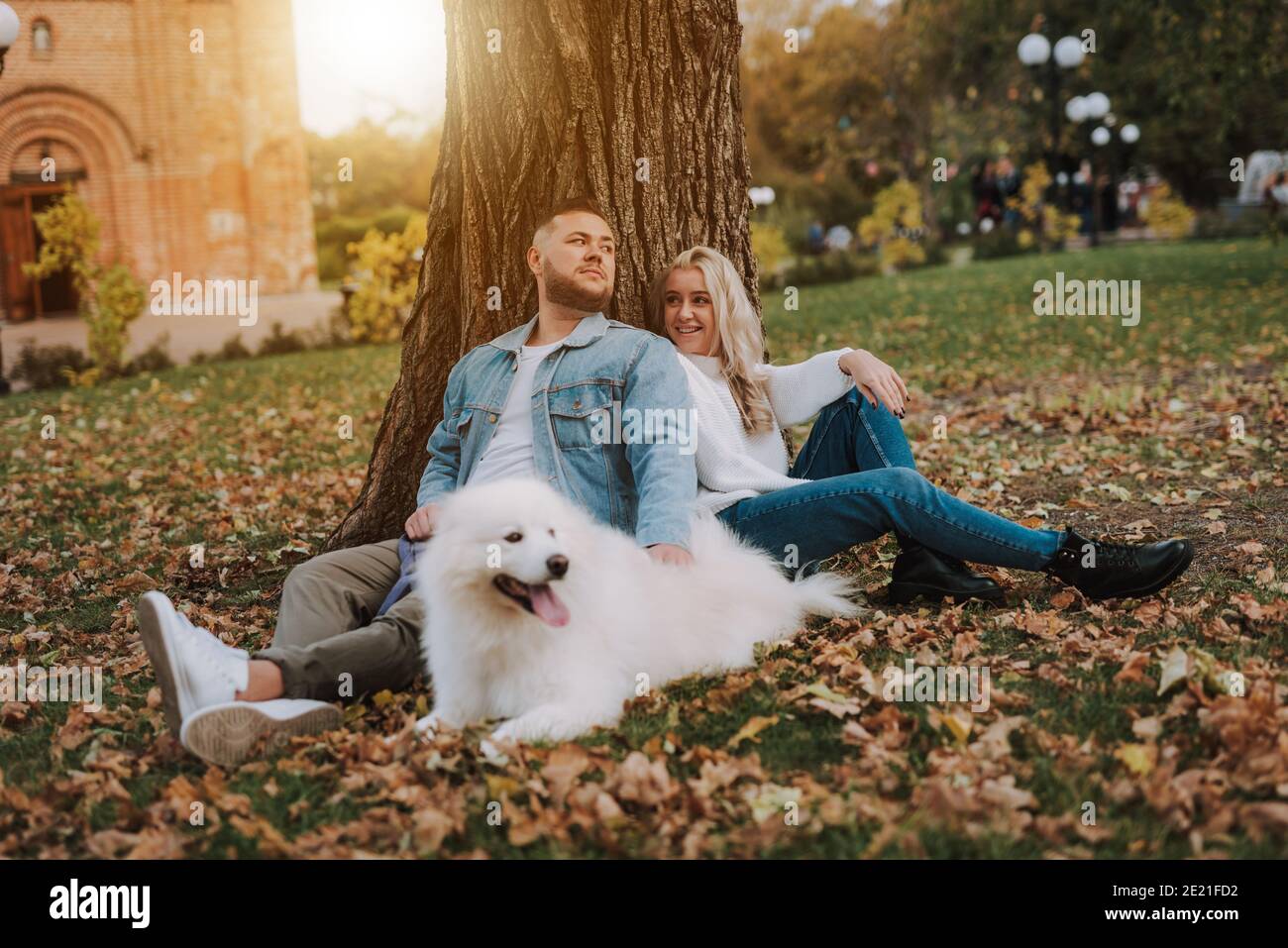 Young smiling female and male with white furry puppy sitting under tree ...