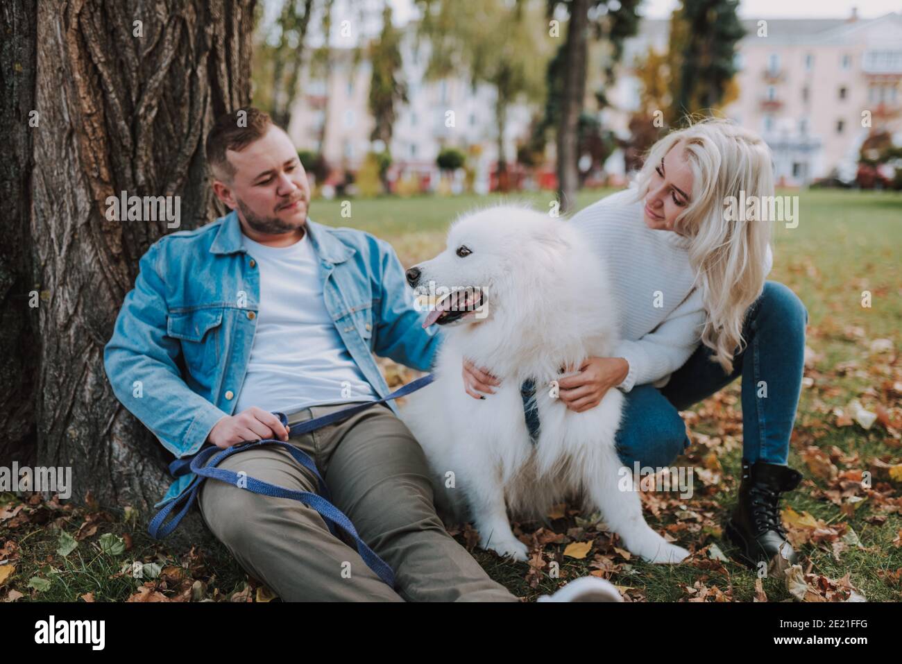 Happy female and male are hugging white furry playful puppy samoyed ...