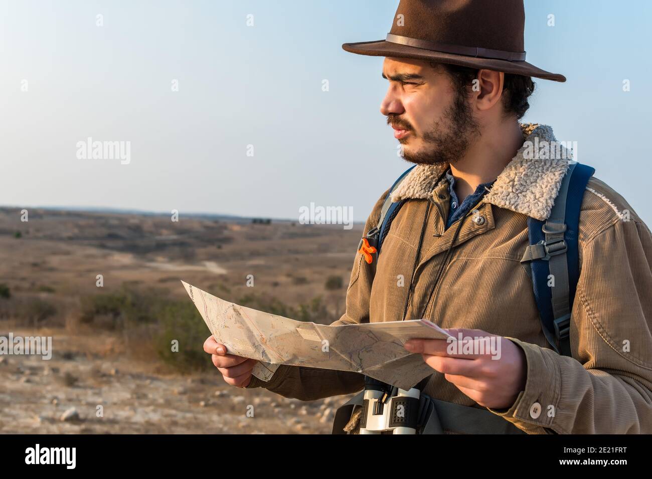 Hiker holding a traveler's map and looking at the horizon to find a ...
