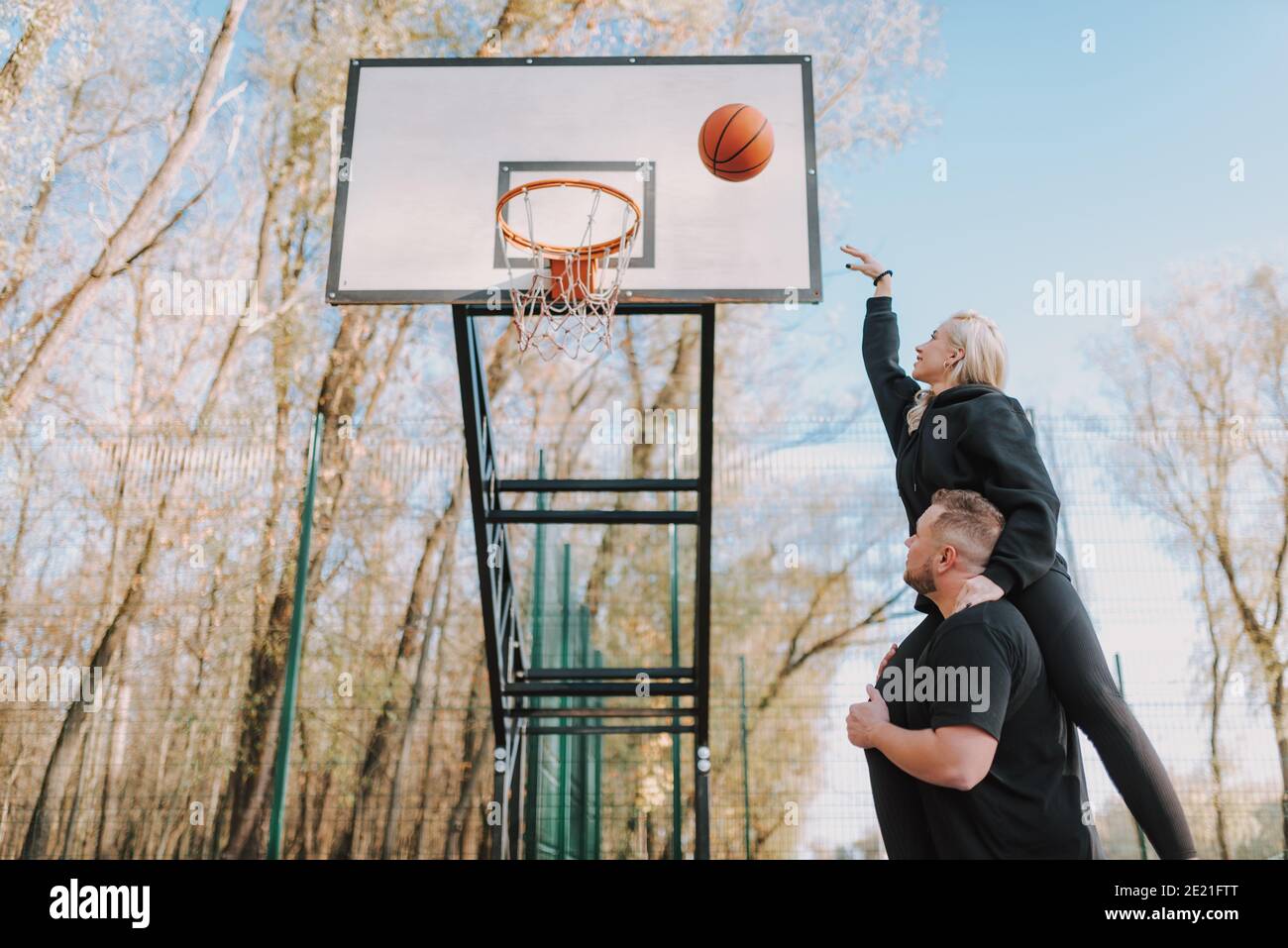Happy pretty woman throwing ball into basket while sitting on boyfriend ...