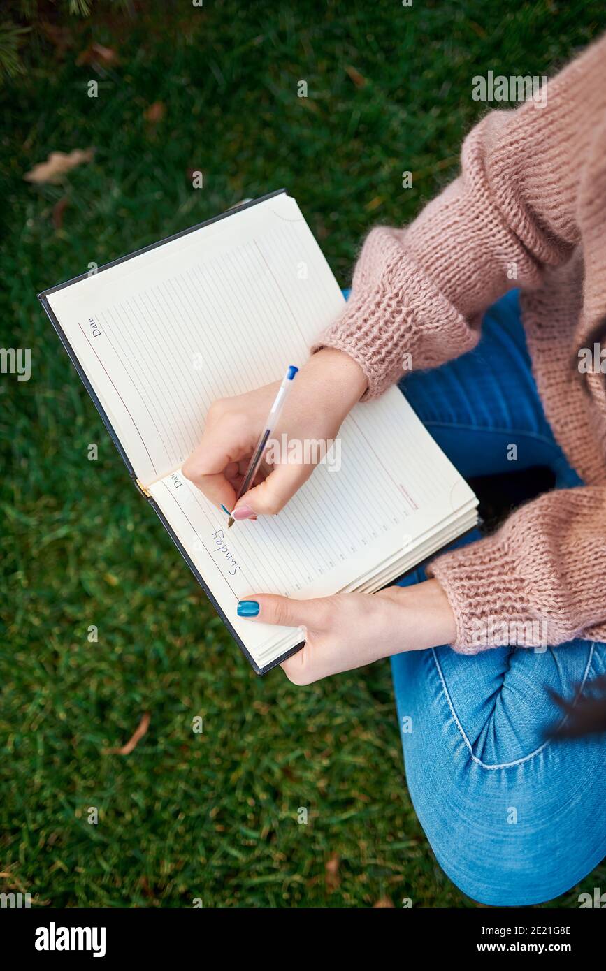 Top view of young lady in casual clothing writing something down to her ...