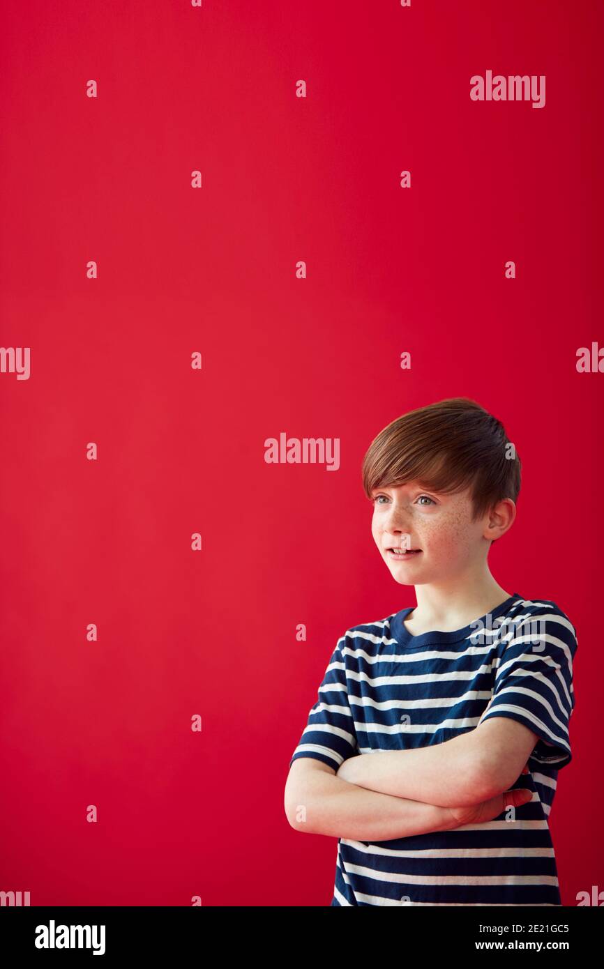 Portrait Of Young Boy With Folded Arms Against Red Studio Background ...