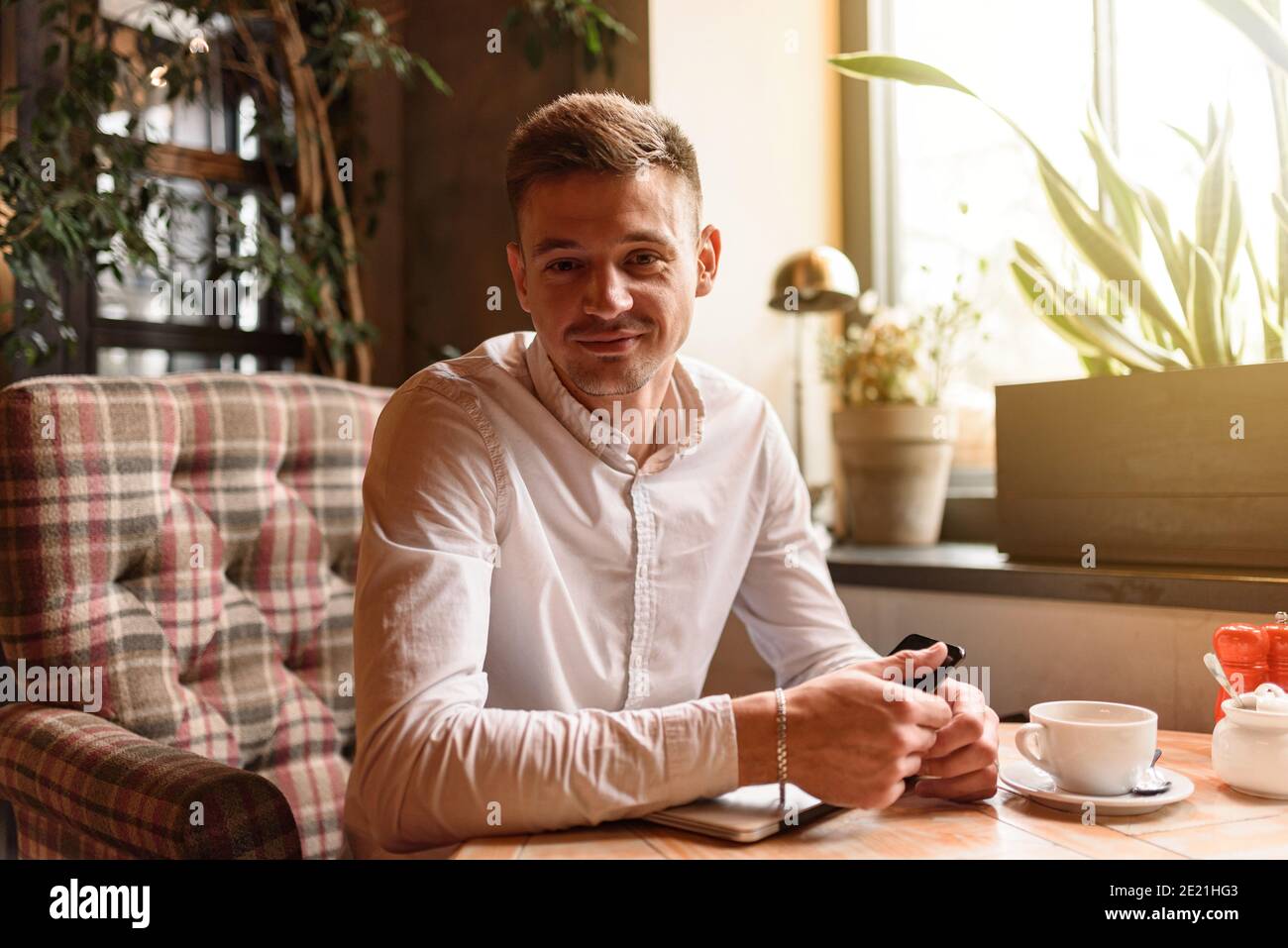 Waist up of smiling handsome guy wearing white shirt while sitting in ...