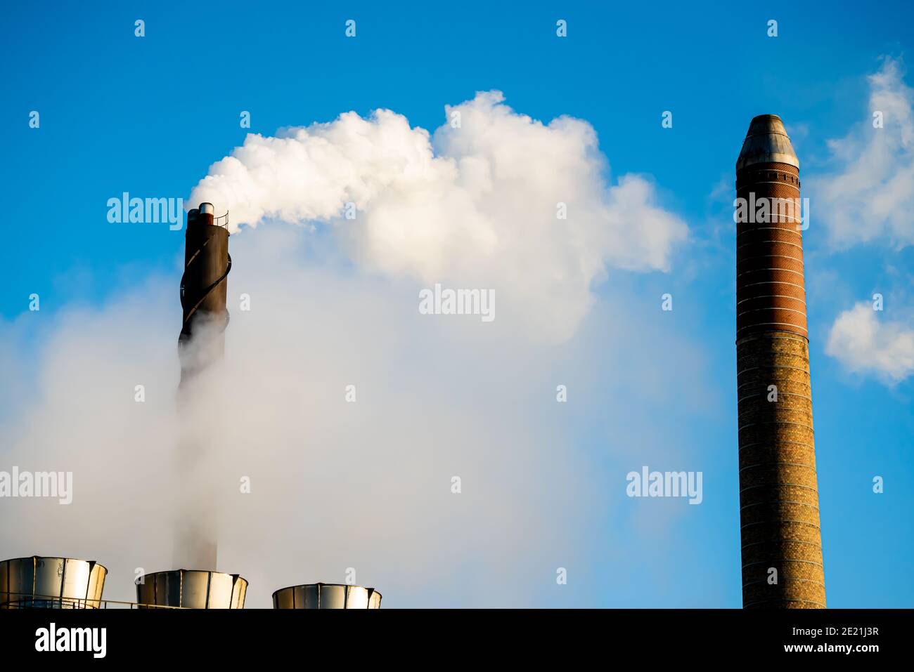 Industrial smoke stacks putting out steam and smoke on a clear blue sky ...