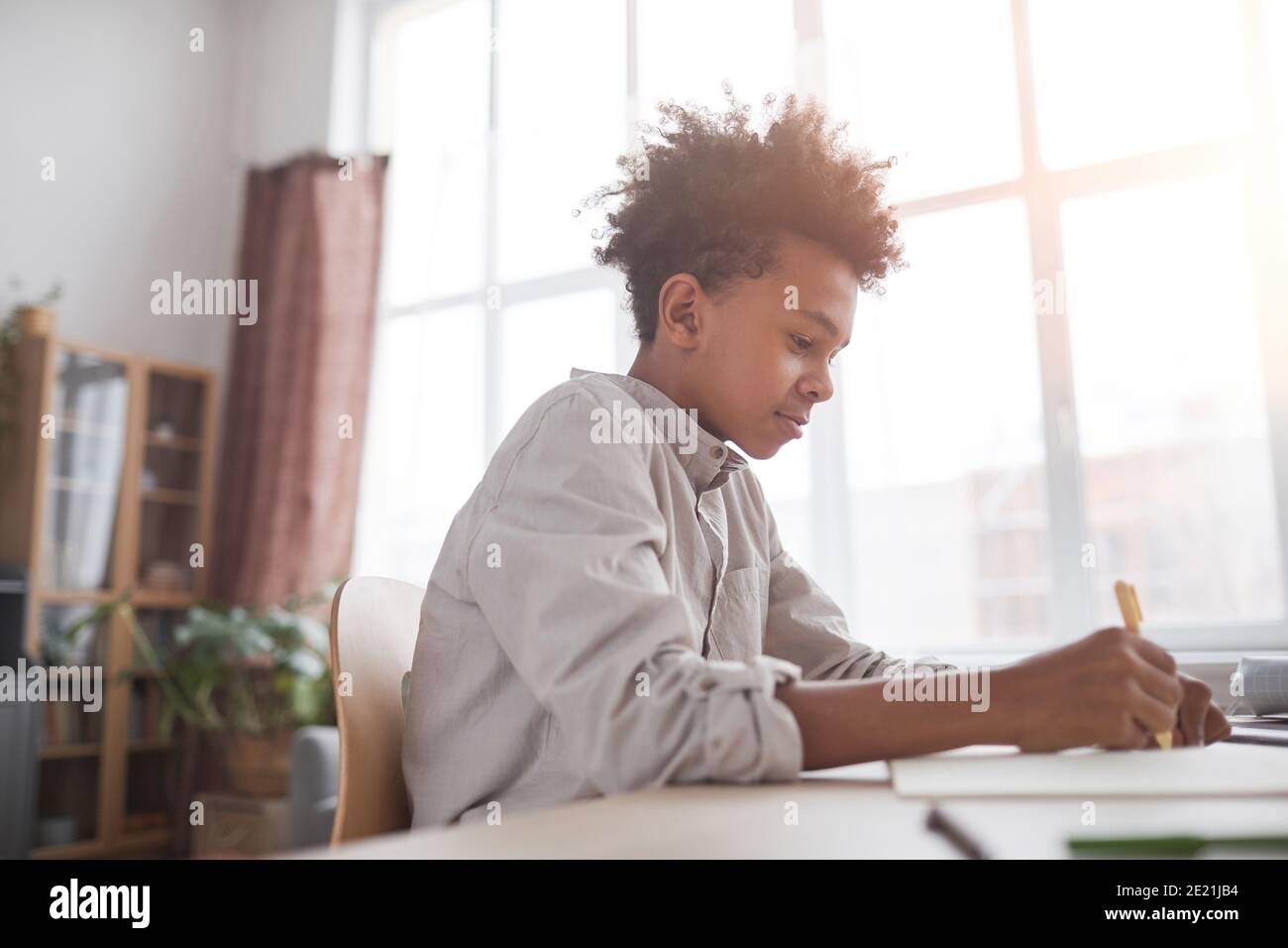 Side view portrait of teenage African-American boy doing homework while ...