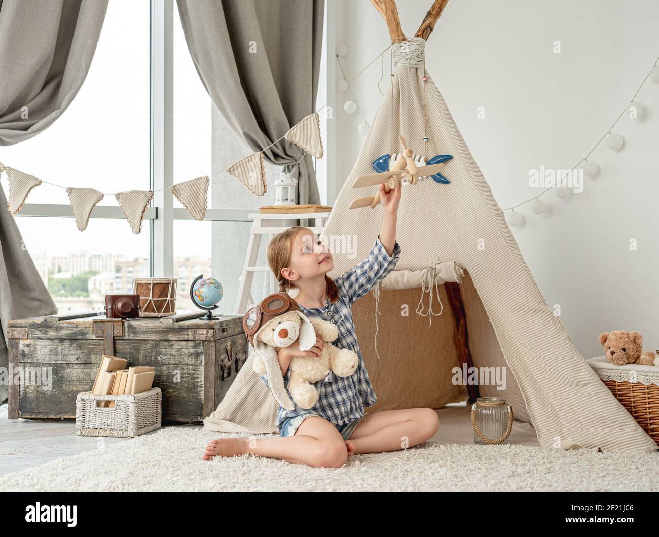 Happy little girl flying wooden plane sitting in room with retro things ...