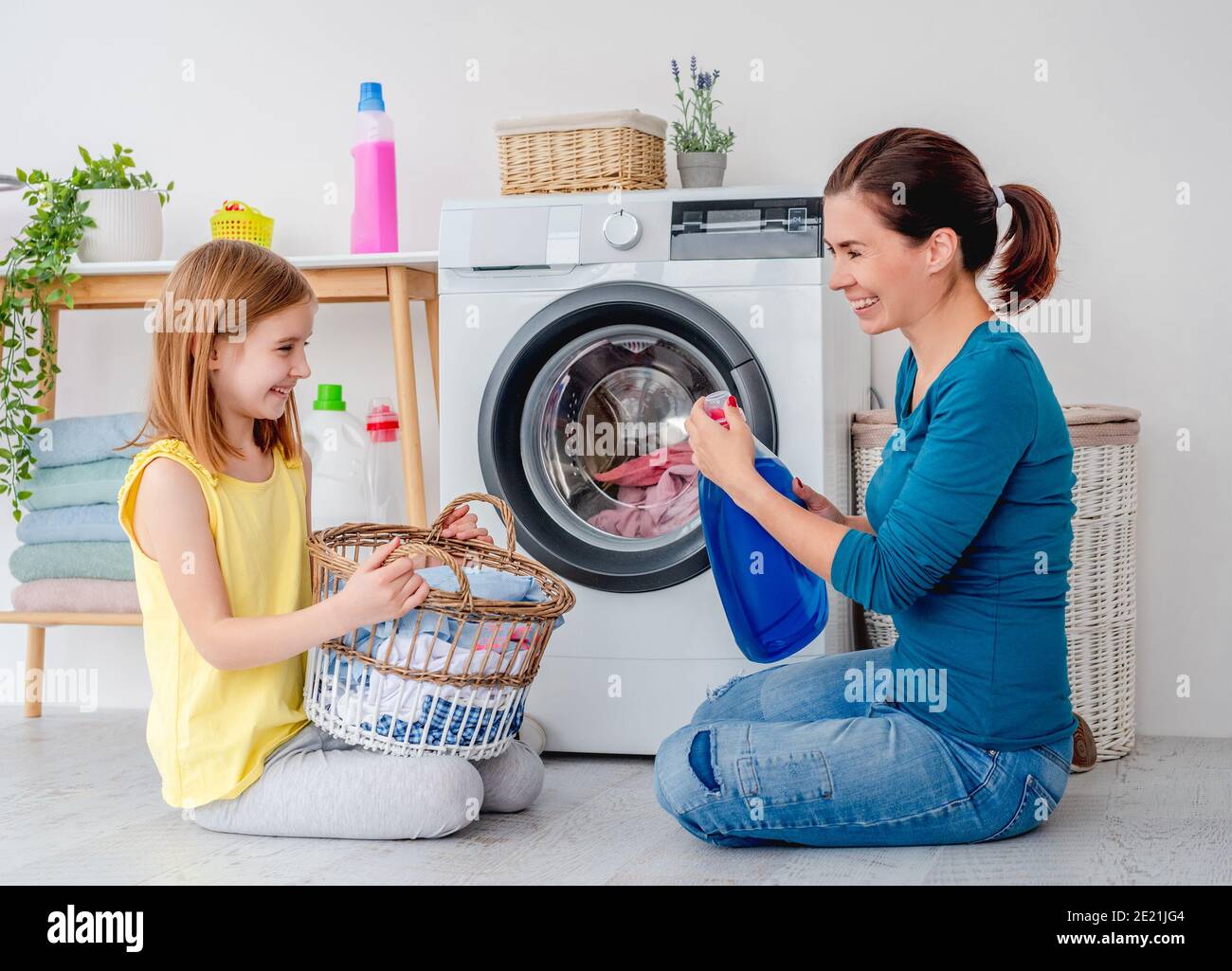 Happy mother and little daughter washing clothes using machine in light ...