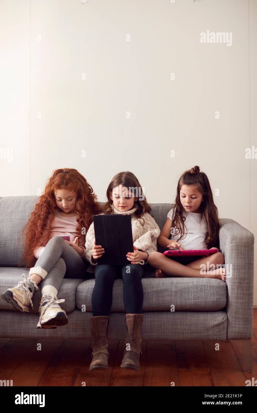 Group Of Girls With Friends Sitting On Sofa At Home Playing On Digital ...