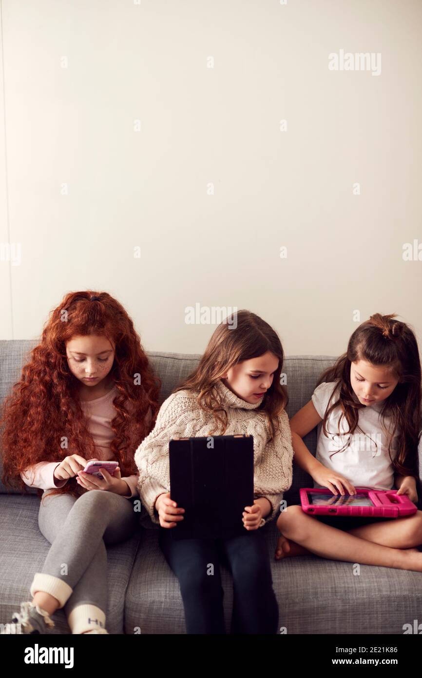 Group Of Girls With Friends Sitting On Sofa At Home Playing On Digital ...