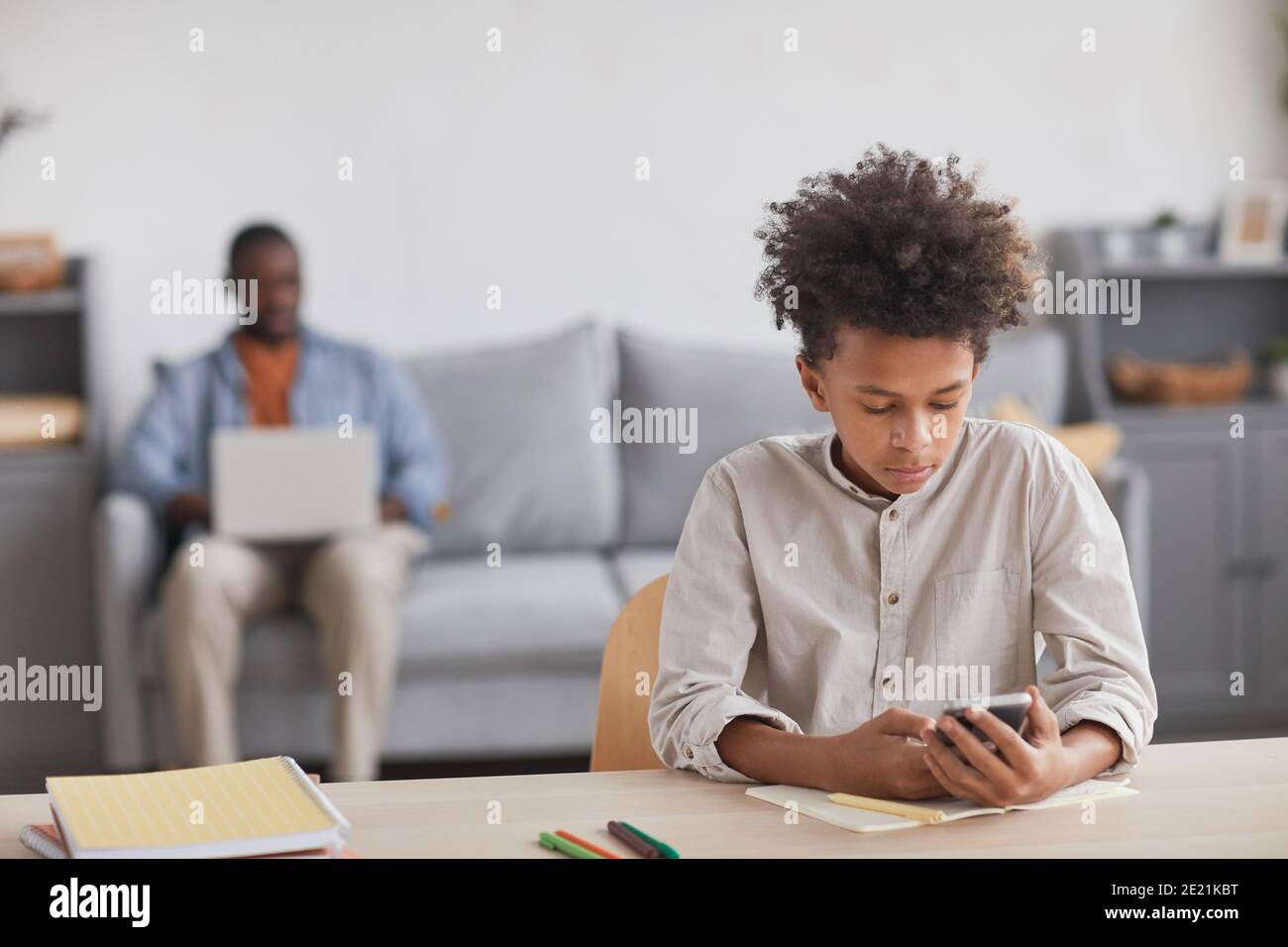 Portrait of teenage African-American boy using smartphone while doing ...